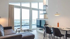 Uma sala de estar moderna com sofá, mesa de jantar, cadeiras, televisão e grandes janelas com vista para uma ponte.