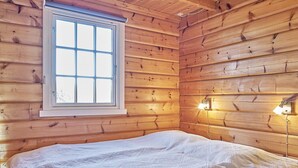 Quarto de cabana de madeira com uma cama, uma janela e duas luzes fixadas na parede.