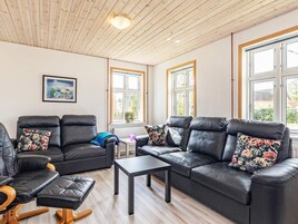 Sala de estar com dois sofás de couro preto, uma mesa de centro de madeira e um quadro pendurado na parede.