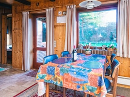 Interior de madeira com mesa de jantar, cadeiras e janela com vista para vegetação.