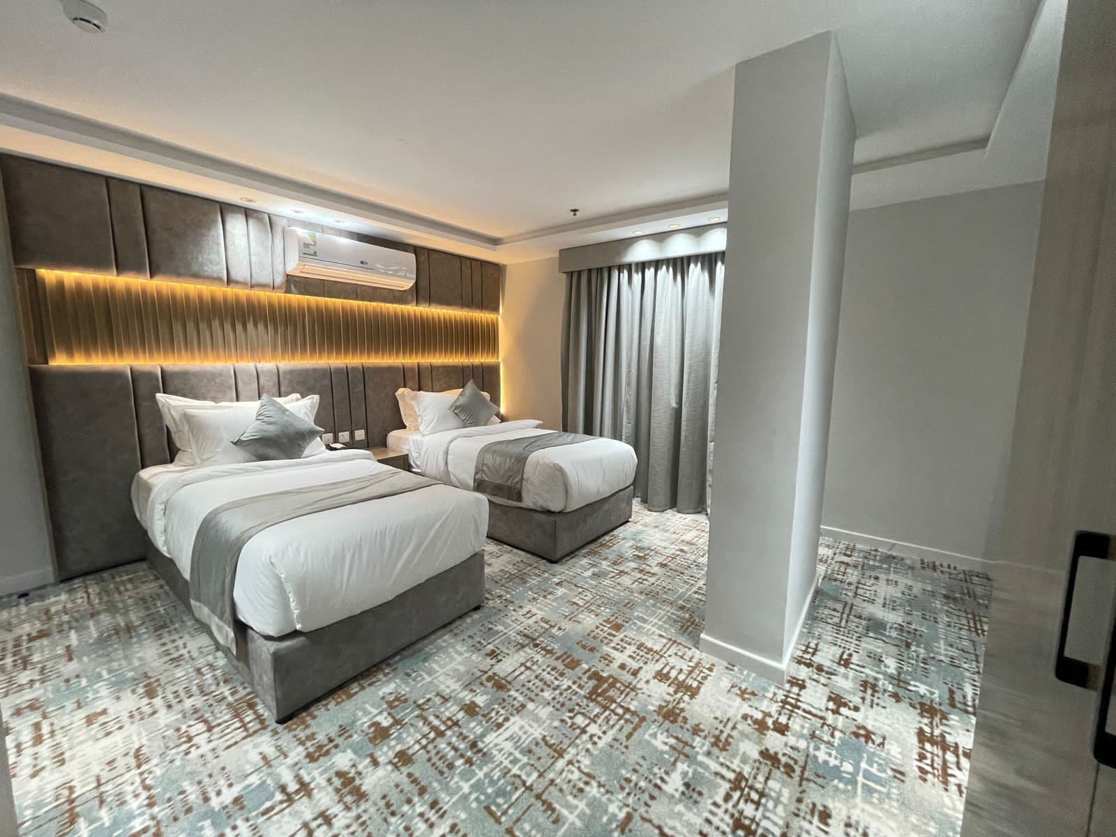Quarto de hotel moderno com duas camas, ar condicionado de parede grande e carpete estampado.