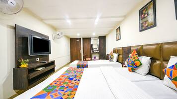 Quarto de hotel com duas camas, televisão, ventoinha e um tapete colorido.