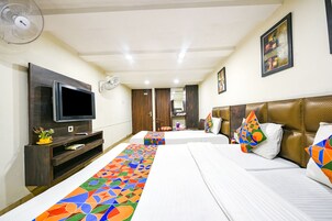 Quarto de hotel com duas camas, televisão, ventoinha e um tapete colorido.