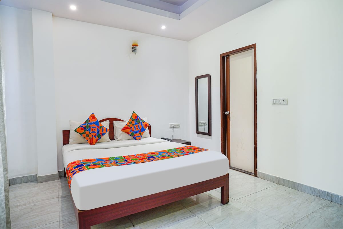 Quarto com cama, mesa de cabeceira, espelho e porta.
