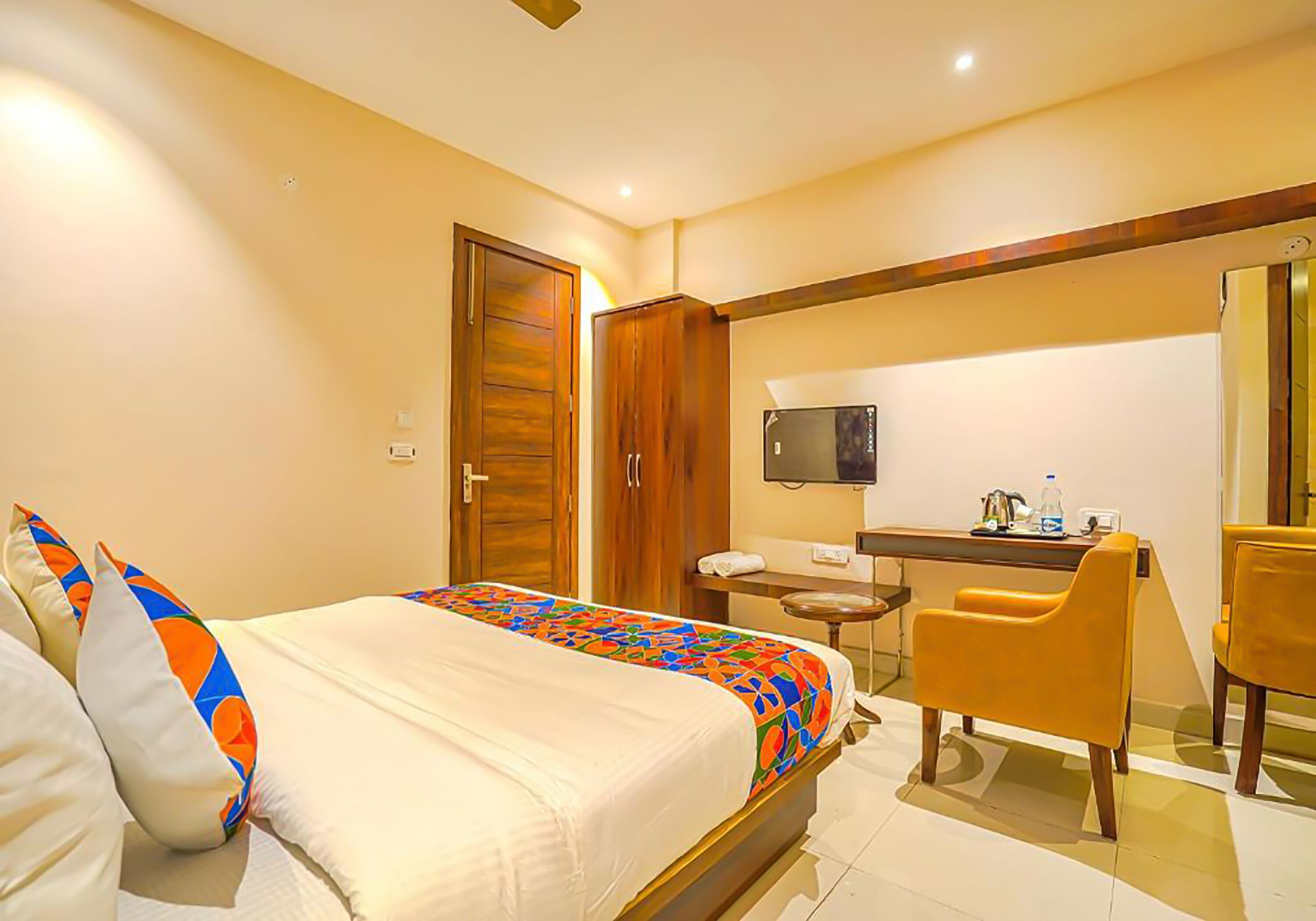 Quarto de hotel com cama, escrivaninha, cadeira e televisão.