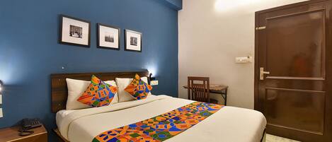 Quarto de hotel com uma cama, mesa de cabeceira, porta de madeira e uma cadeira.