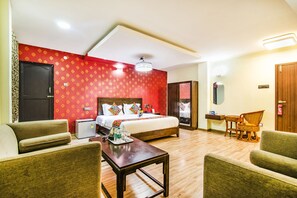 Quarto de hotel com cama, escrivaninha, duas cadeiras e uma mesa pequena.