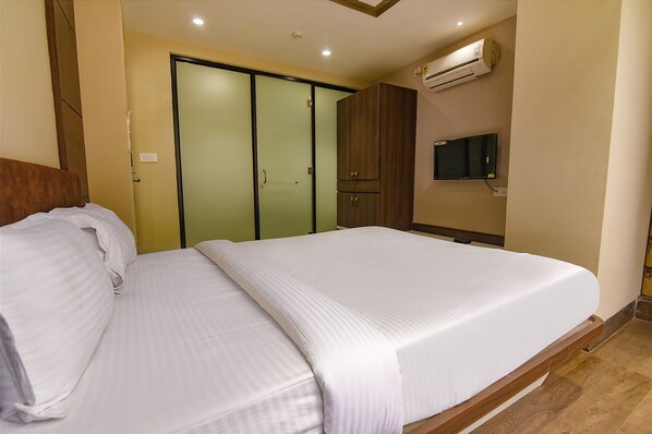 Quarto de hotel com uma cama grande, um guarda-roupa e uma televisão.