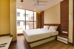 Quarto de hotel com uma cama, uma escrivaninha, um ventilador de teto e uma janela com cortinas.