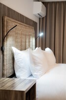 Uma cama bem arrumada com lençóis brancos, um painel de cabeceira texturizado e uma mesa de cabeceira com abajur.