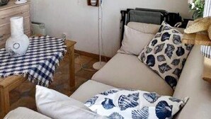 Quarto com sofá, ventilador, toalha de mesa xadrez e prateleira na parede com um vaso.