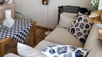 Quarto com sofá, ventilador, toalha de mesa xadrez e prateleira na parede com um vaso.