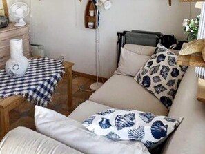 Quarto com sofá, ventilador, toalha de mesa xadrez e prateleira na parede com um vaso.