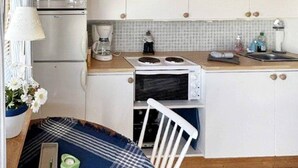 Cozinha compacta com armários brancos, micro-ondas, máquina de café e uma pequena área de jantar com uma cadeira e mesa.