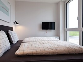 Quarto com duas camas, televisão de tela plana fixada na parede, abajur e janela com vista para o exterior.