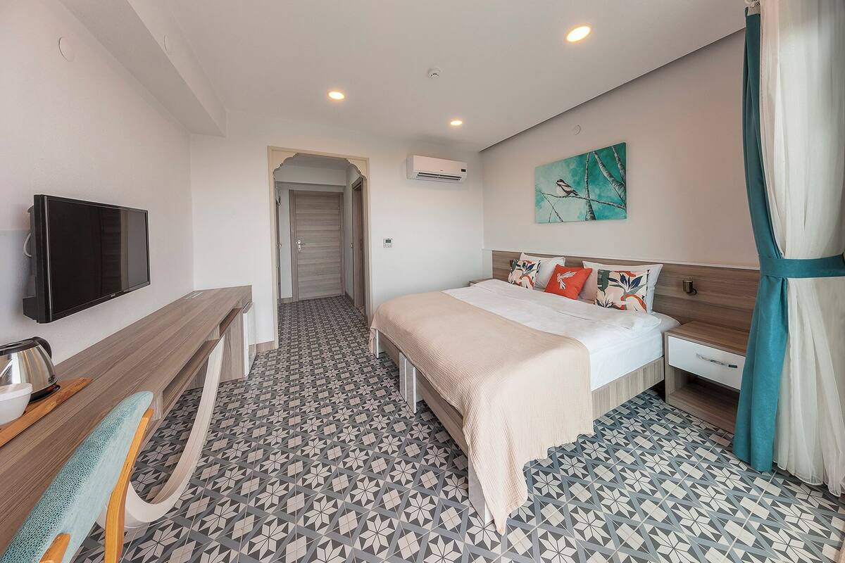 Quarto de hotel com cama, escrivaninha, televisão e um quadro na parede.