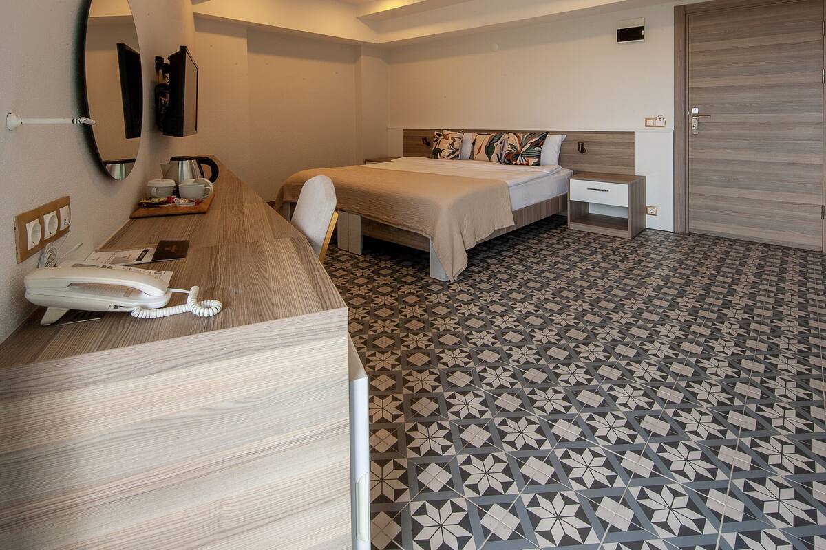 Quarto de hotel com cama, mesa de cabeceira e escrivaninha com telefone.
