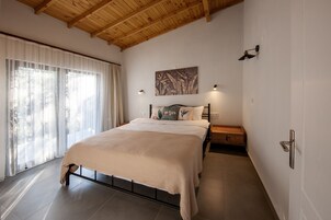 Quarto com cama, mesa de cabeceira, teto de madeira, janela com cortinas e uma obra de arte na parede.