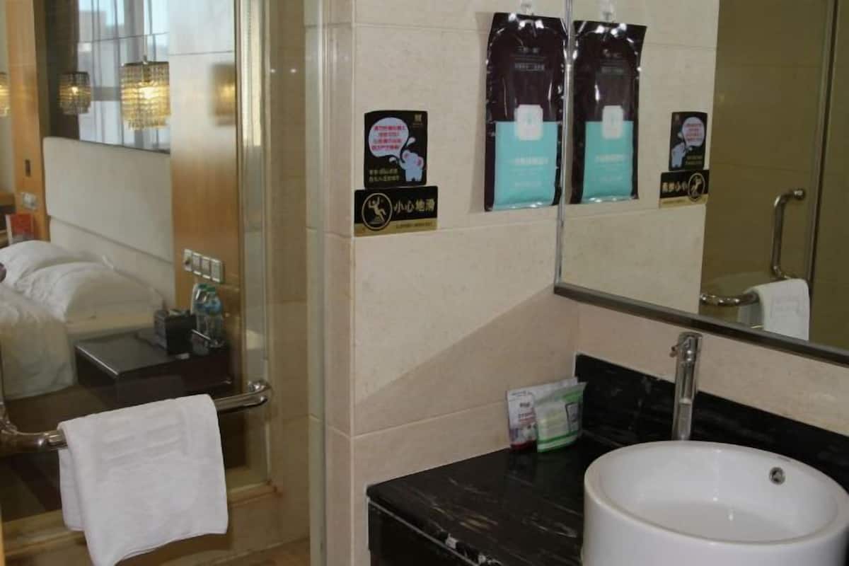 Um banheiro de hotel com um espelho grande, pia branca e artigos de higiene pessoal no balcão.