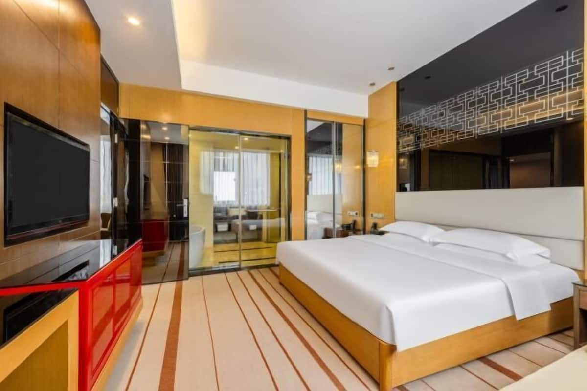 Quarto de hotel moderno com uma cama grande, televisão e porta de vidro que dá para uma varanda.