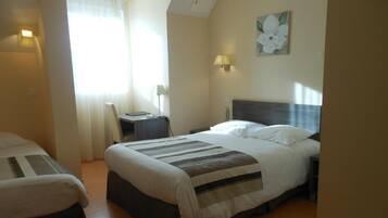 Quarto de hotel com duas camas, uma mesa, uma cadeira e uma luminária.
