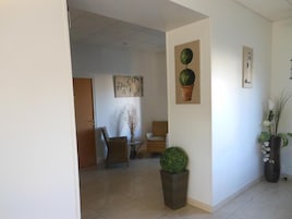 Um corredor com porta, mobiliário de vime, planta em vaso e obras de arte nas paredes.
