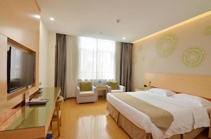 Quarto de hotel com cama, televisão, escrivaninha e área de estar com mesa e cadeiras.