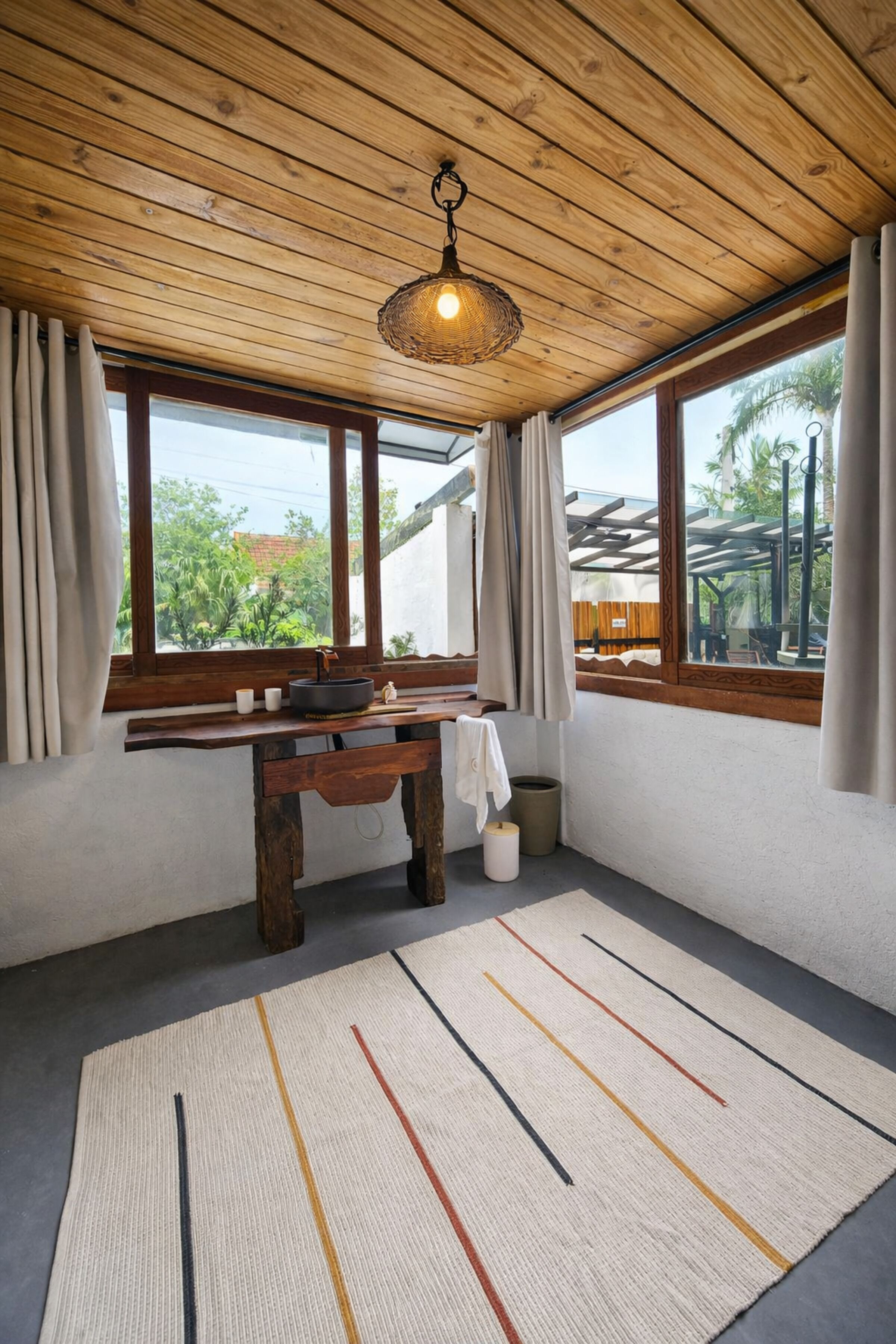 Quarto com teto de madeira, amplas janelas, uma mesa com vela e um tapete colorido.