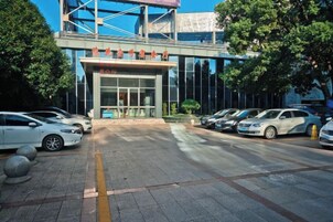 Um edifício com entrada moderna, um estacionamento com vários carros e céu claro.