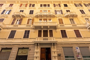 Edifício com várias andares, varandas, persianas e entrada no nível da rua.