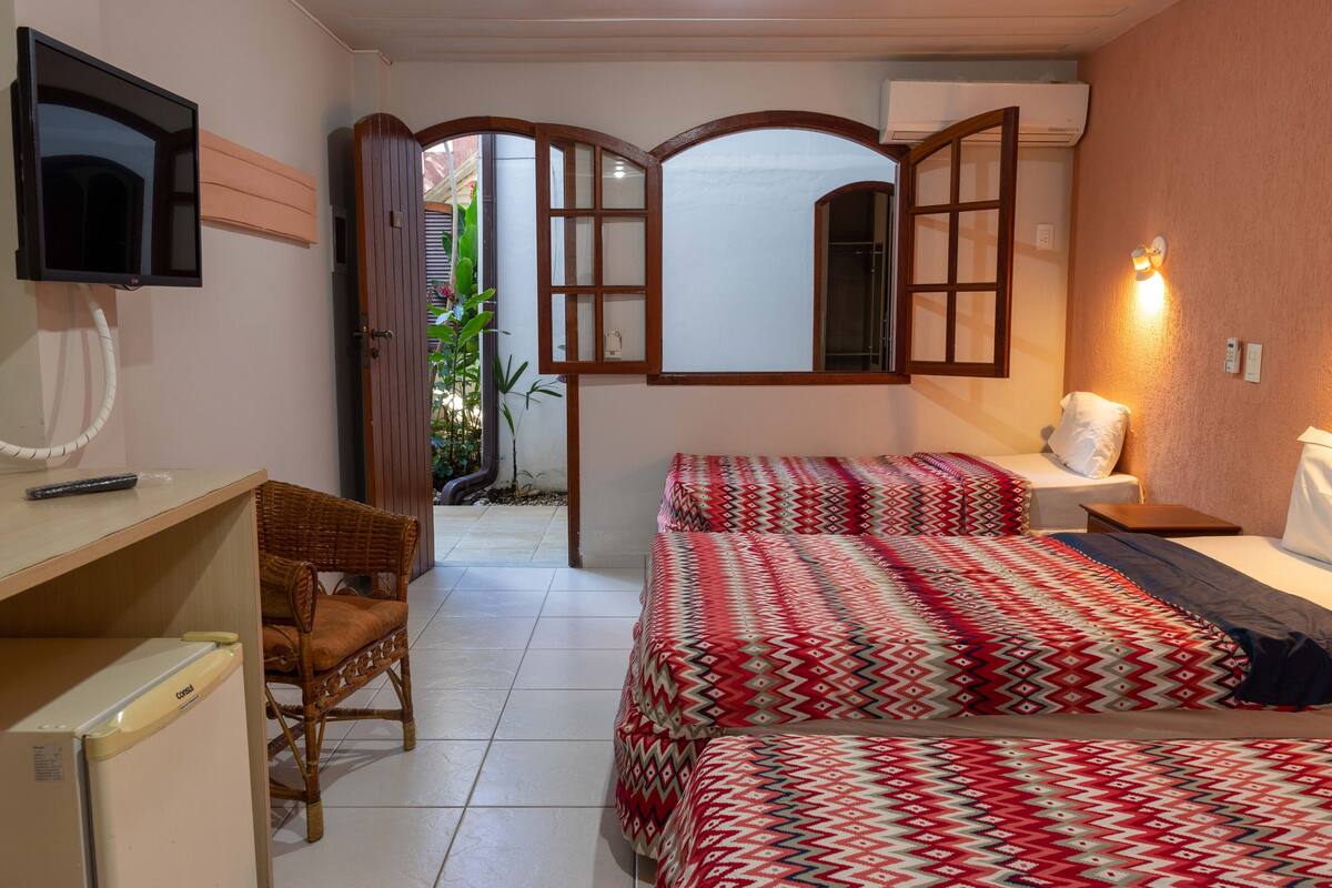Quarto de hotel com duas camas, uma escrivaninha, uma cadeira, uma televisão e um ar condicionado.