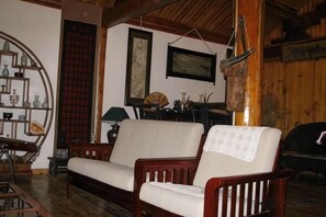 Quarto com sofá de madeira, mesa lateral, luminária e prateleira fixada na parede com objetos decorativos.