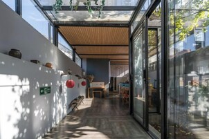 Corredor com parede de vidro, teto de madeira e área de jantar visível através do vidro.