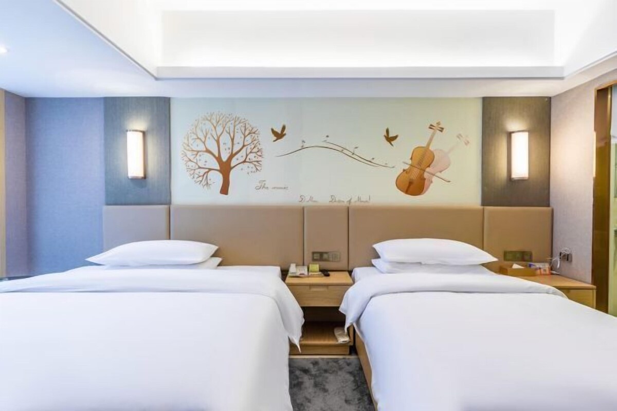 Quarto de hotel com duas camas, um mural na parede e uma mesinha de cabeceira entre elas.