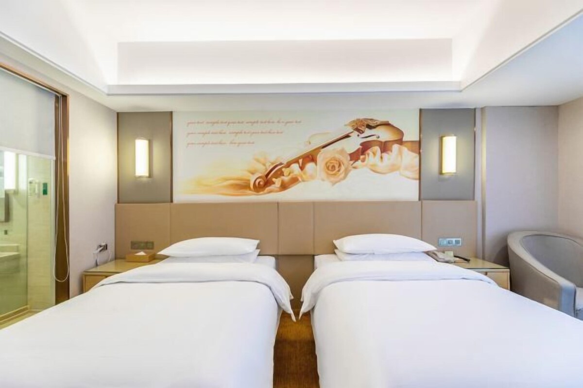 Quarto de hotel com duas camas, um mural grande na parede, chuveiro e um espaço de estar.