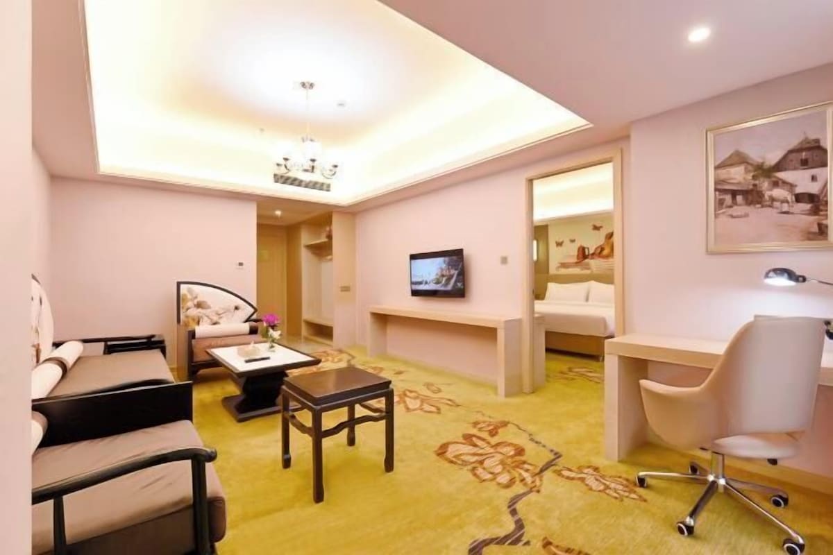 Quarto de hotel moderno com sofá, escrivaninha, cadeira, televisão e lustre.