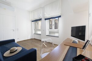 Um quarto com sofá azul, televisão, mesa de madeira e janela com cortinas.
