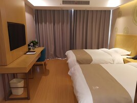 Quarto de hotel com cama, mesa de cabeceira, televisão, escrivaninha, cadeira e cortinas.