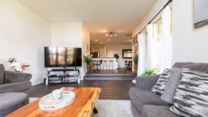 Uma sala de estar moderna com uma mesa de centro de madeira, sofás cinzas e uma televisão de tela plana.