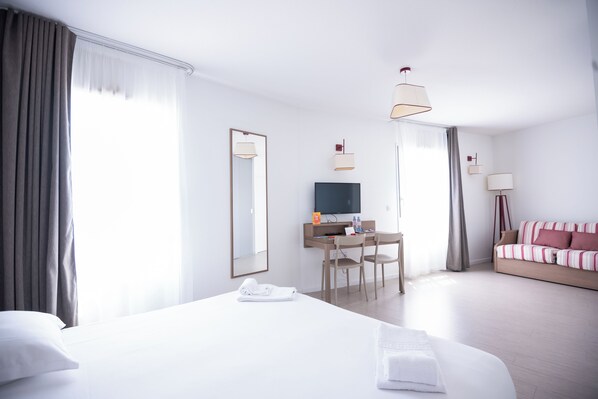 Quarto de hotel com uma cama grande, uma mesa de trabalho com televisão e um sofá.