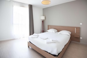 Quarto de hotel moderno com uma cama grande, abajur e vista para o exterior.