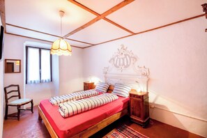 Quarto com cama de madeira, uma cadeira, mesa de cabeceira com abajur e cabeceira decorativa.