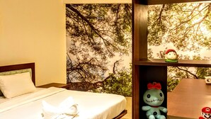 Quarto de hotel com cama, parede com mural de árvore e prateleira com brinquedos macios.