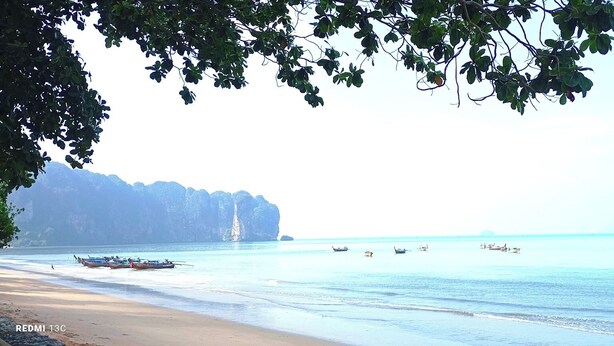 Uma praia com barcos e um penhasco rochoso ao fundo.