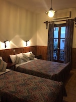 Quarto com duas camas, cabeceira de madeira, luminária pendente e vista para área externa através de uma porta.
