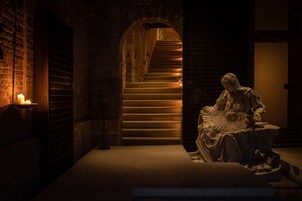 Uma estátua em um salão com pouca luz, com uma escada que leva a uma porta.