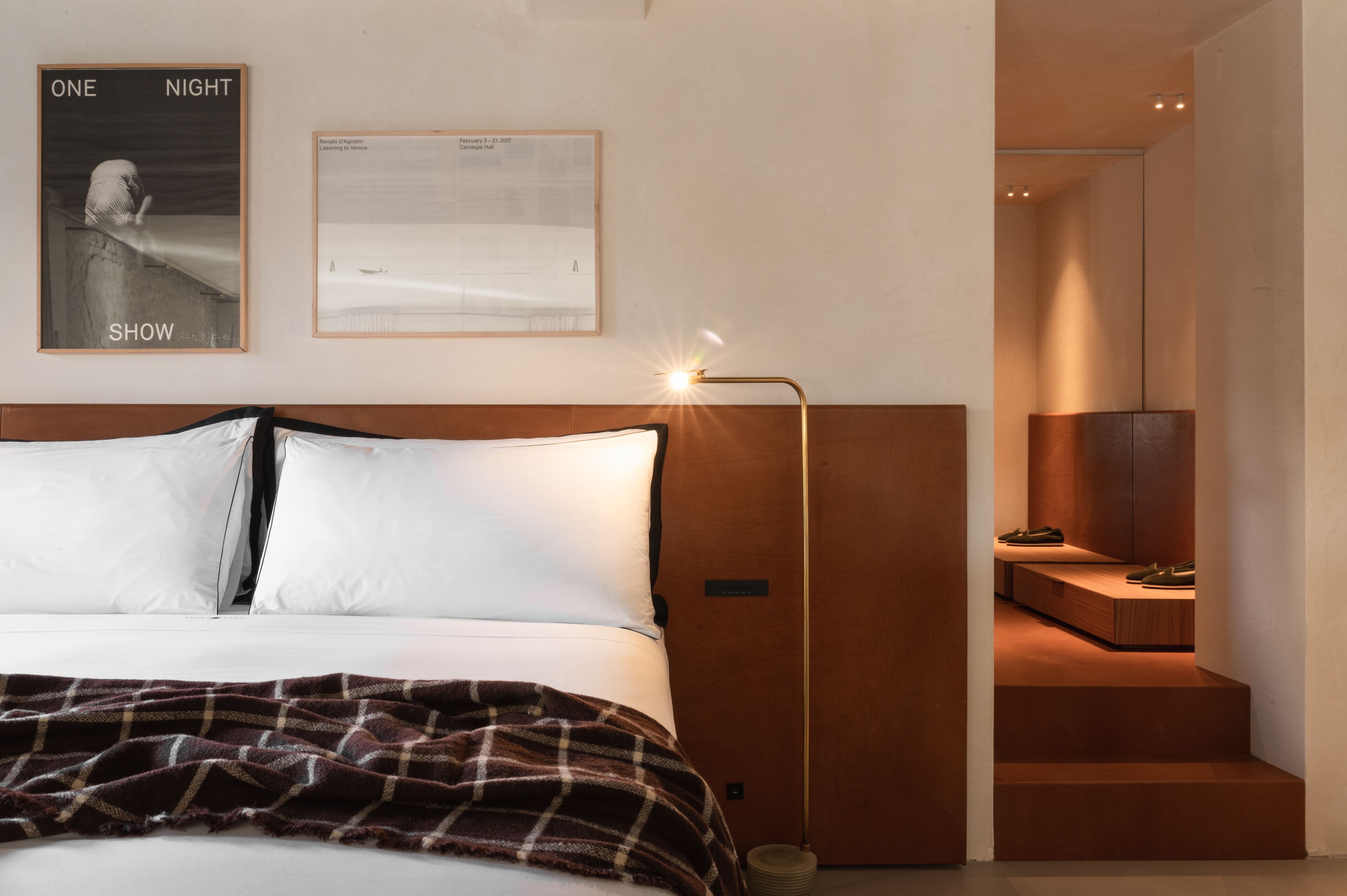Quarto de hotel moderno com uma cama grande, mesa de cabeceira, quadro emoldurado e escada que leva a uma varanda.