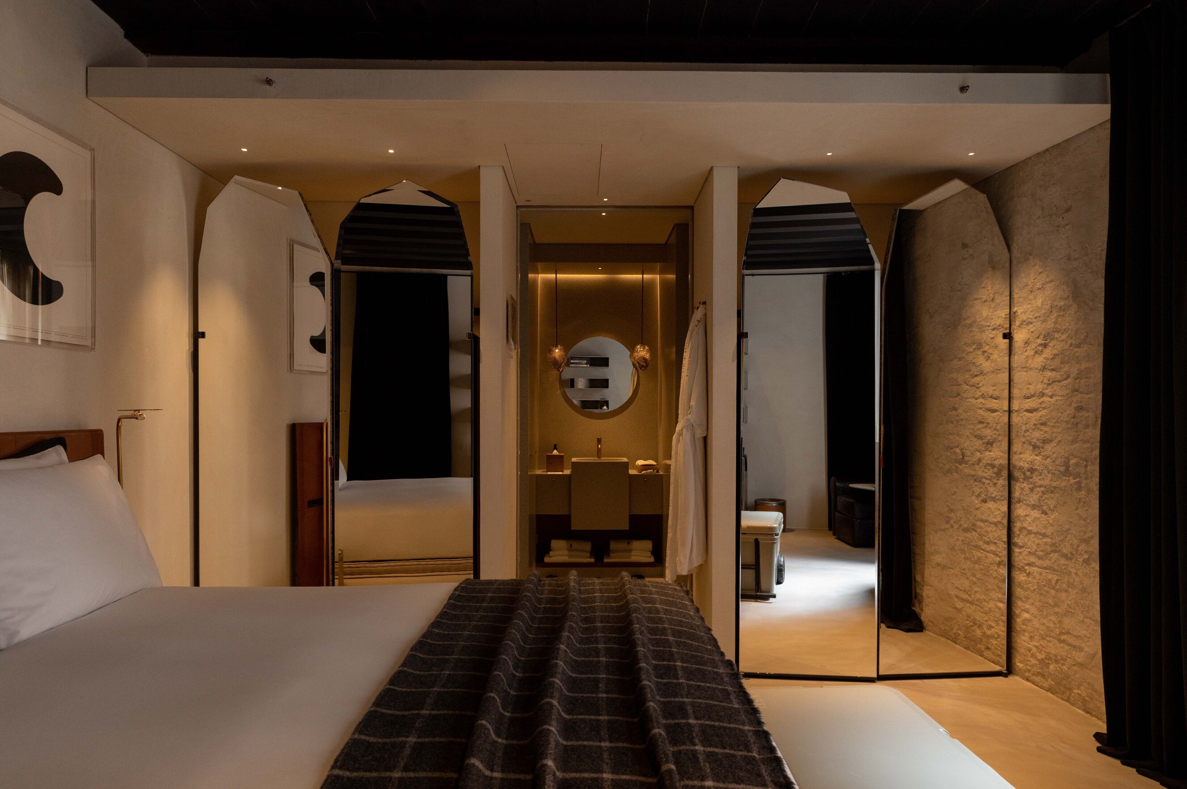 Quarto de hotel moderno com uma cama grande, um espelho, um banheiro com espelho redondo e um closet espaçoso.