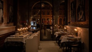 Restaurante com iluminação suave, mesas preparadas para refeições, com vista para um edifício histórico através de um painel de vidro.