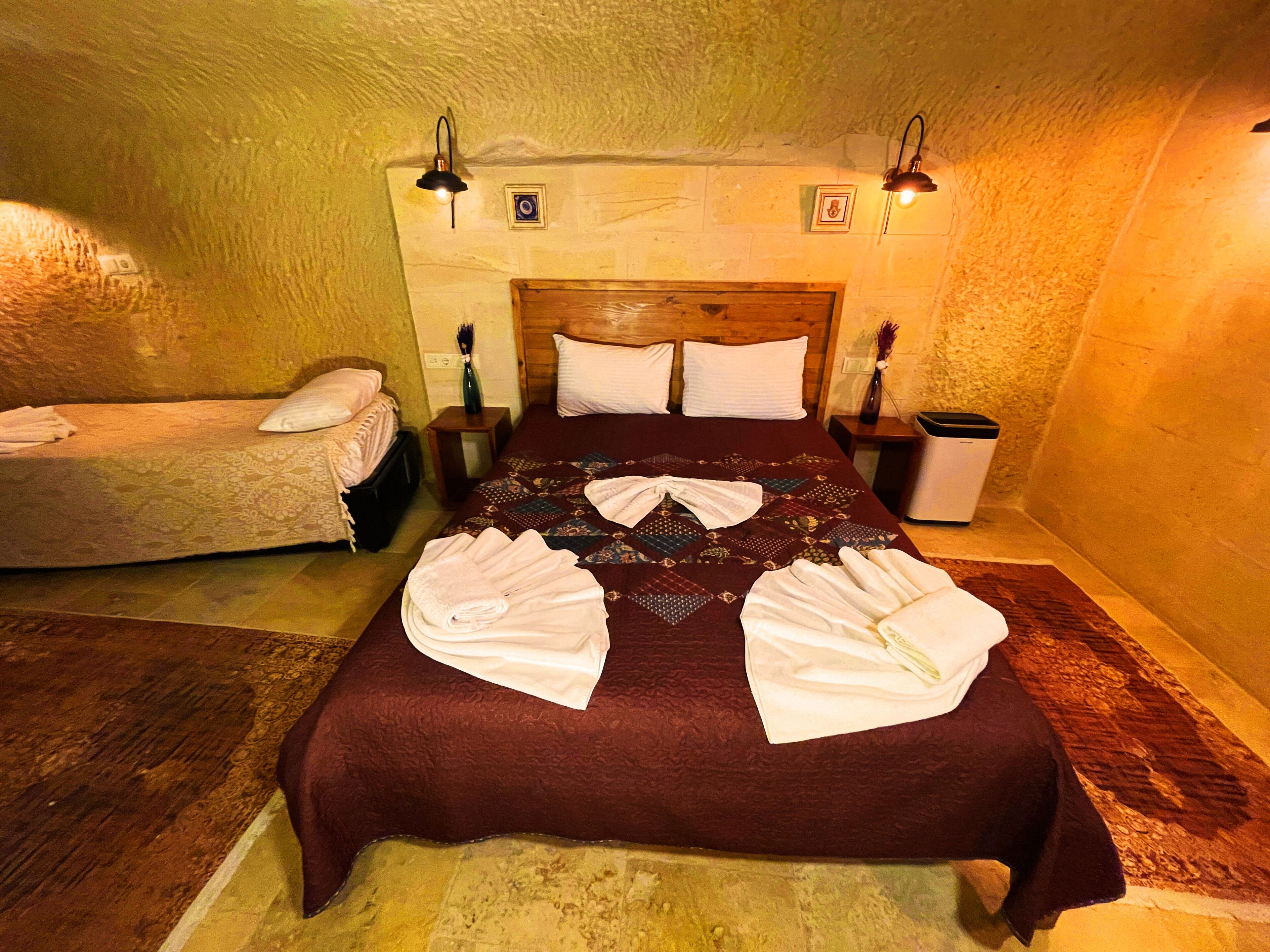 Quarto de hotel com uma cama grande, duas mesas de cabeceira, um criado-mudo e uma pequena mesa com um vaso.